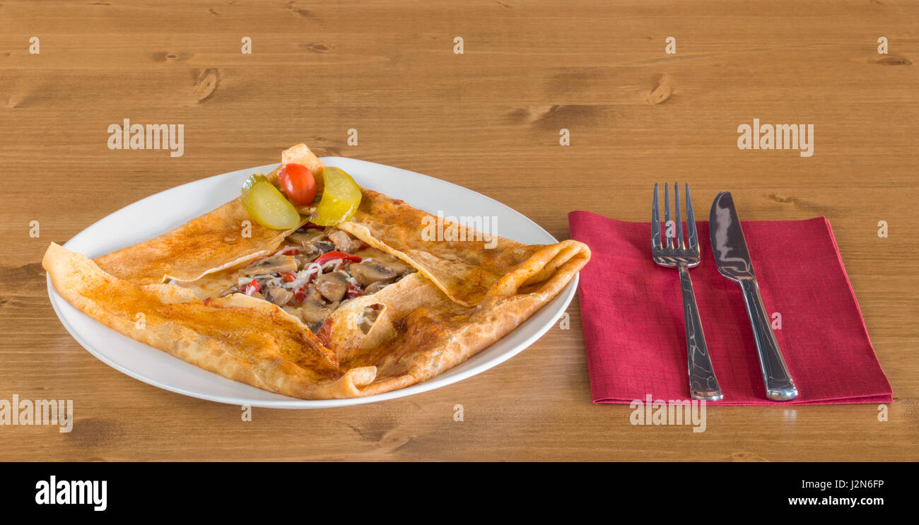 Delicious crepe with mushroom served on a white plate on a wooden table ...