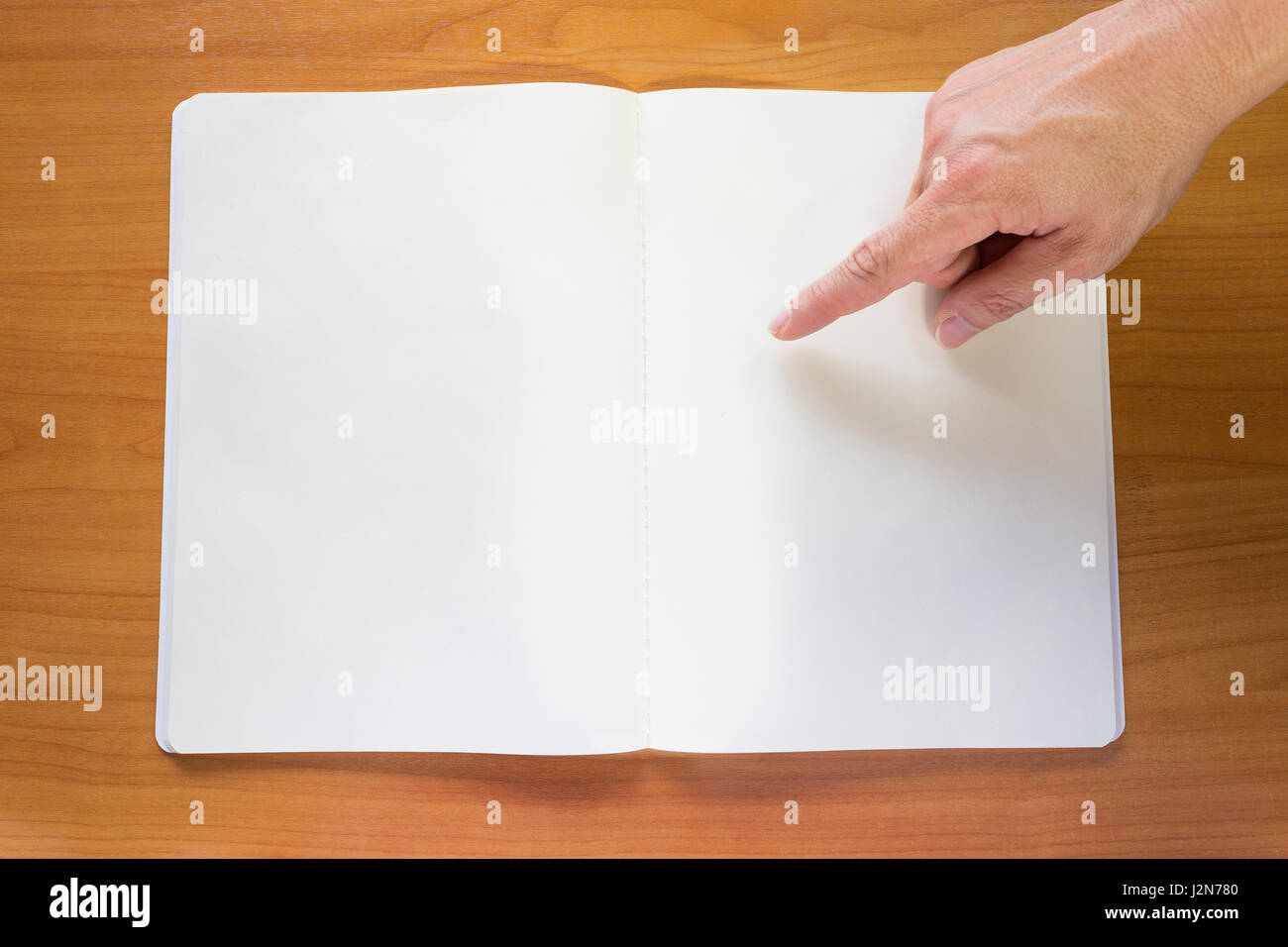 single hand with index finger pointing at blank white paper notebook ...