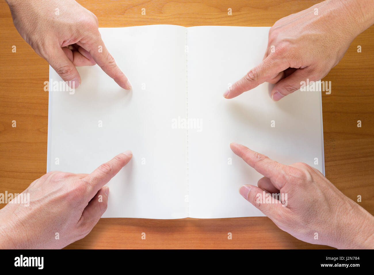 Four hands with finger pointing at blank white paper notebook on wood ...