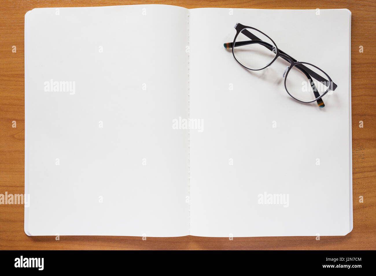 Bland note book with eyeglasses on top of wood table Stock Photo - Alamy