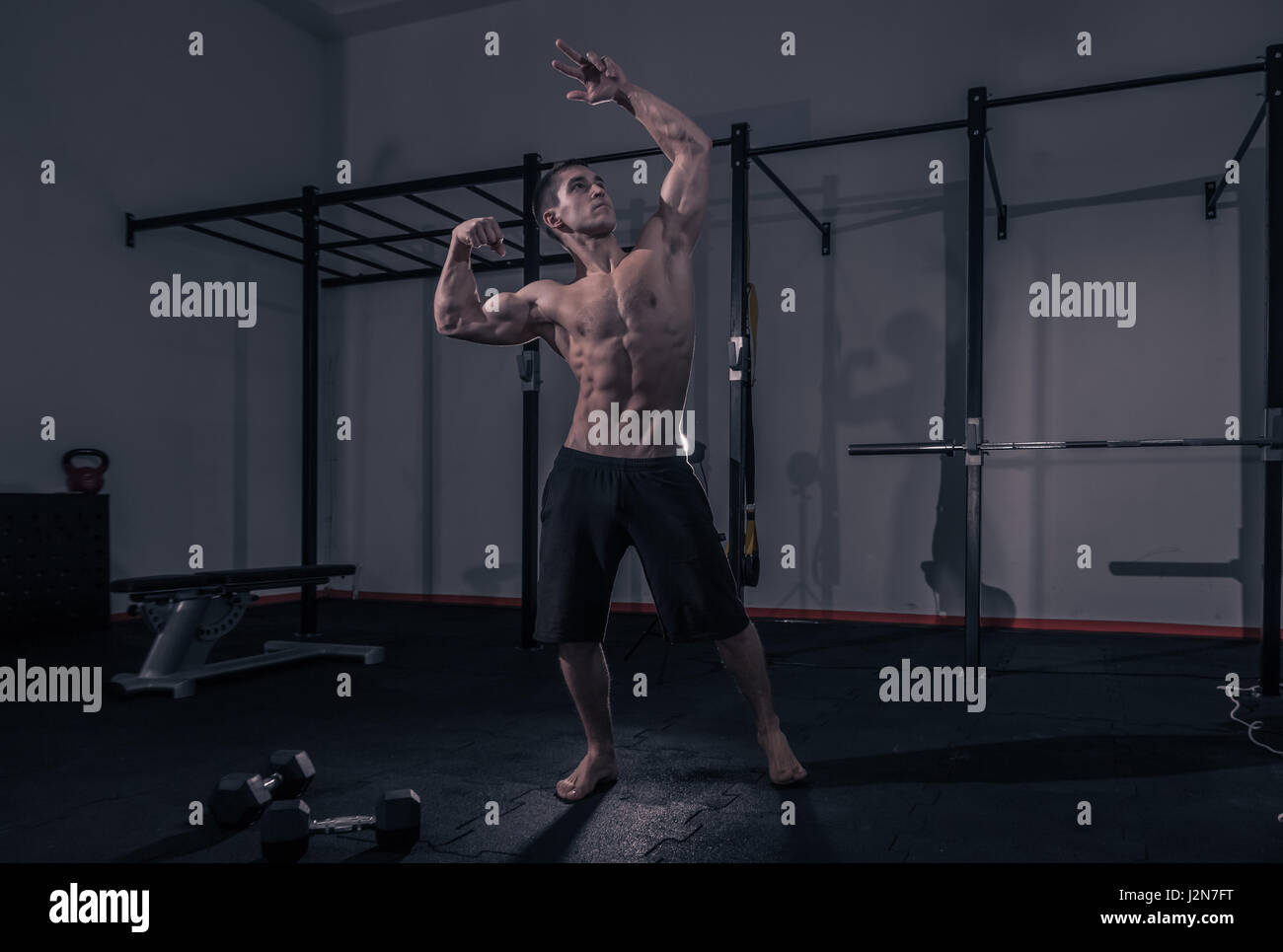 one young man, bodybuilder muscular shirtless, dark gym indoors, arms ...