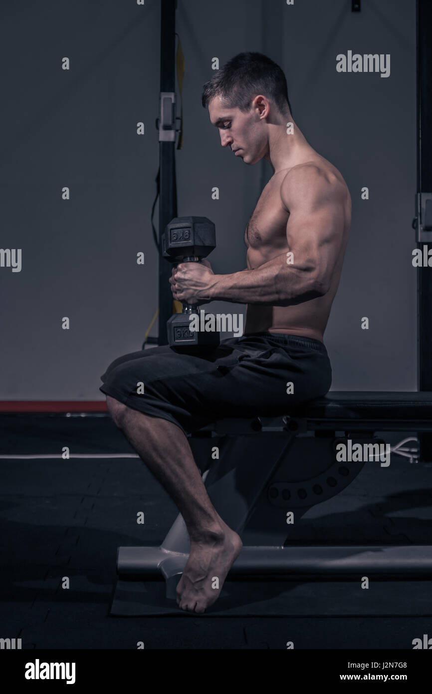 one young man, bodybuilder sitting, flat bench, dumbbell posing ...