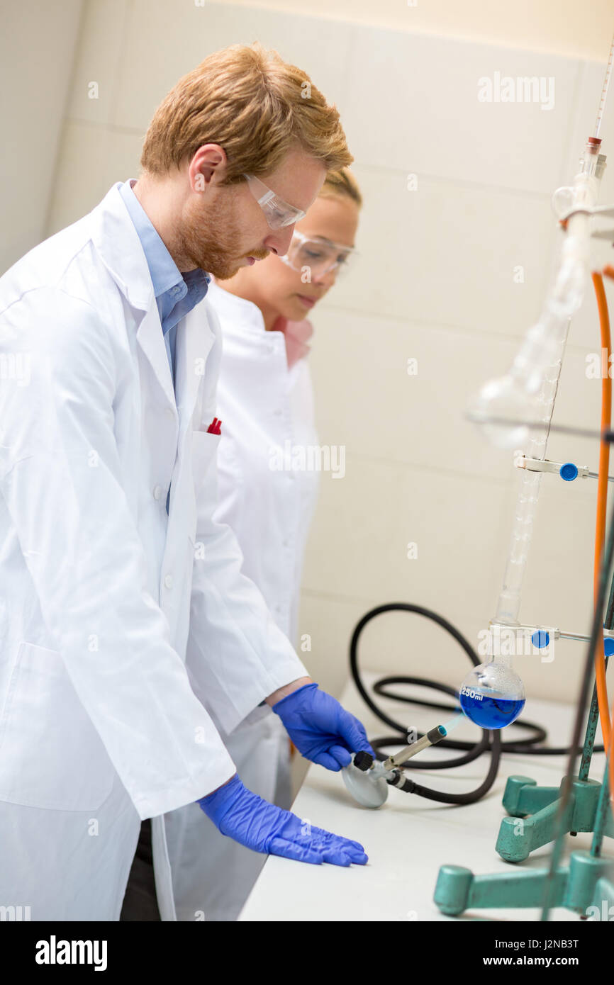 Couple of chemists heat blue liquid with laboratory burner in chemistry ...