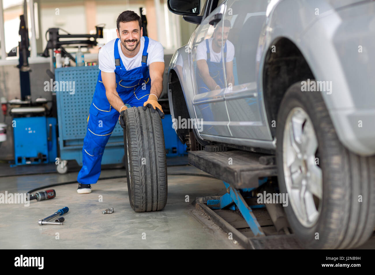 mechanic hands in blue uniform pushing a black tyre in a workshop Stock ...