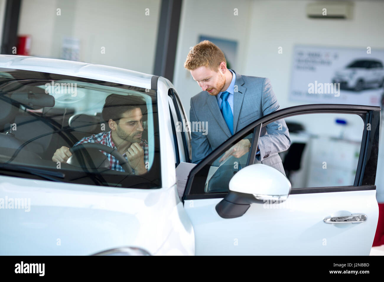 young men looking with car dealer at car in dealership Stock Photo - Alamy