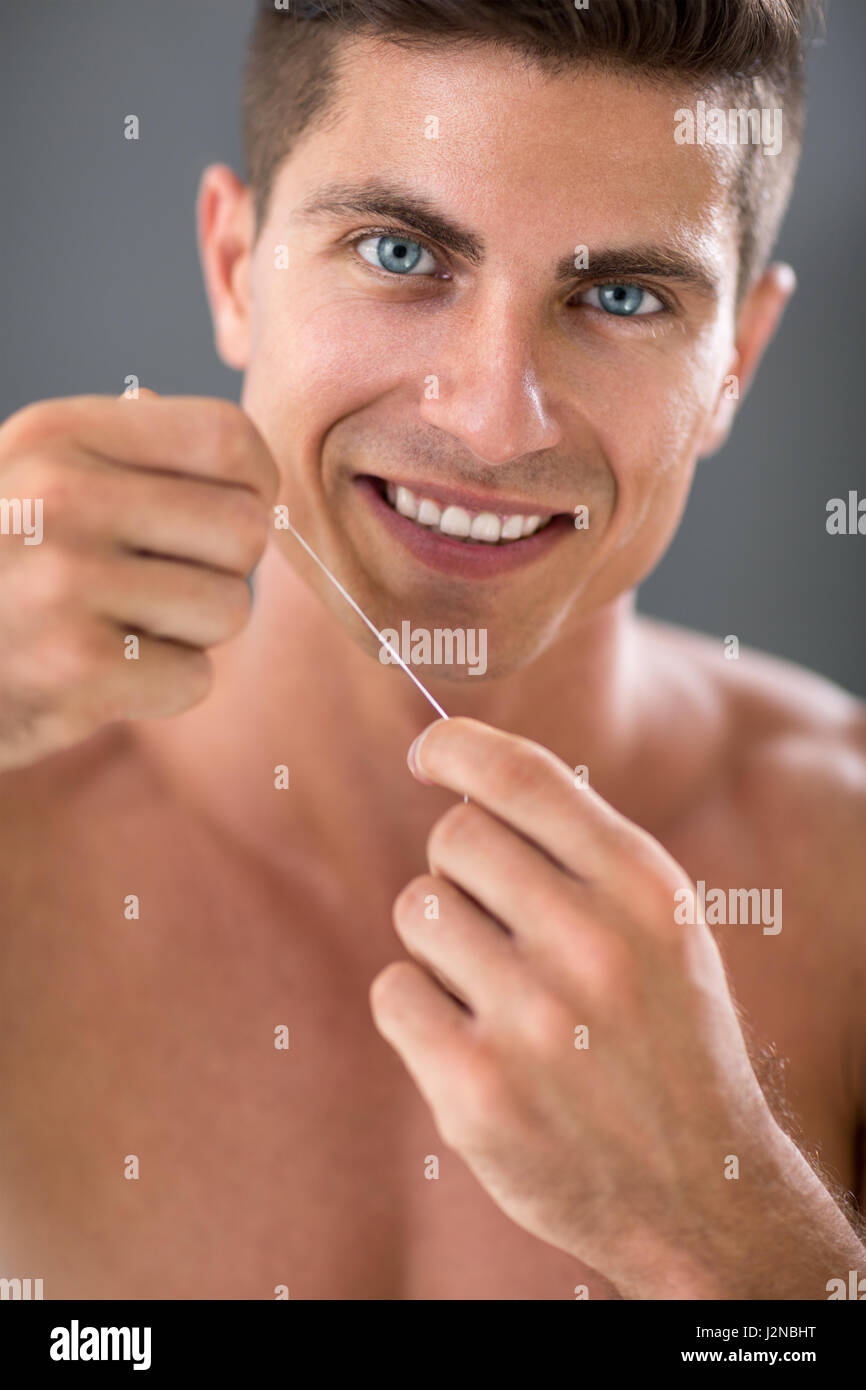 handsome young shirtless man cleaning his teeth with dental floss and ...