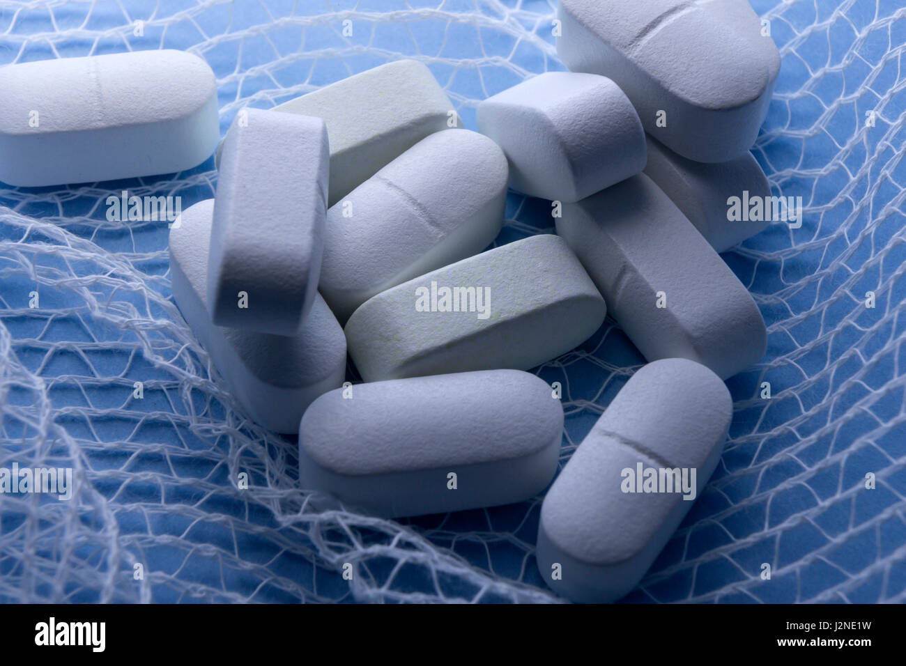 Some white pills wrapped in gauze on a blue background Stock Photo - Alamy