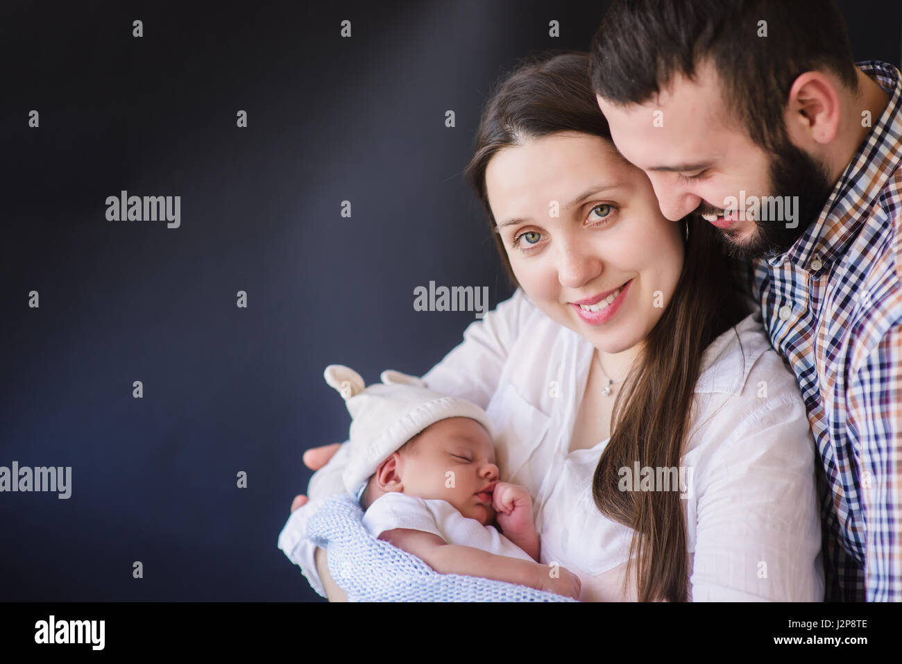 Portrait of happy parents with their newborn baby on a dark background ...