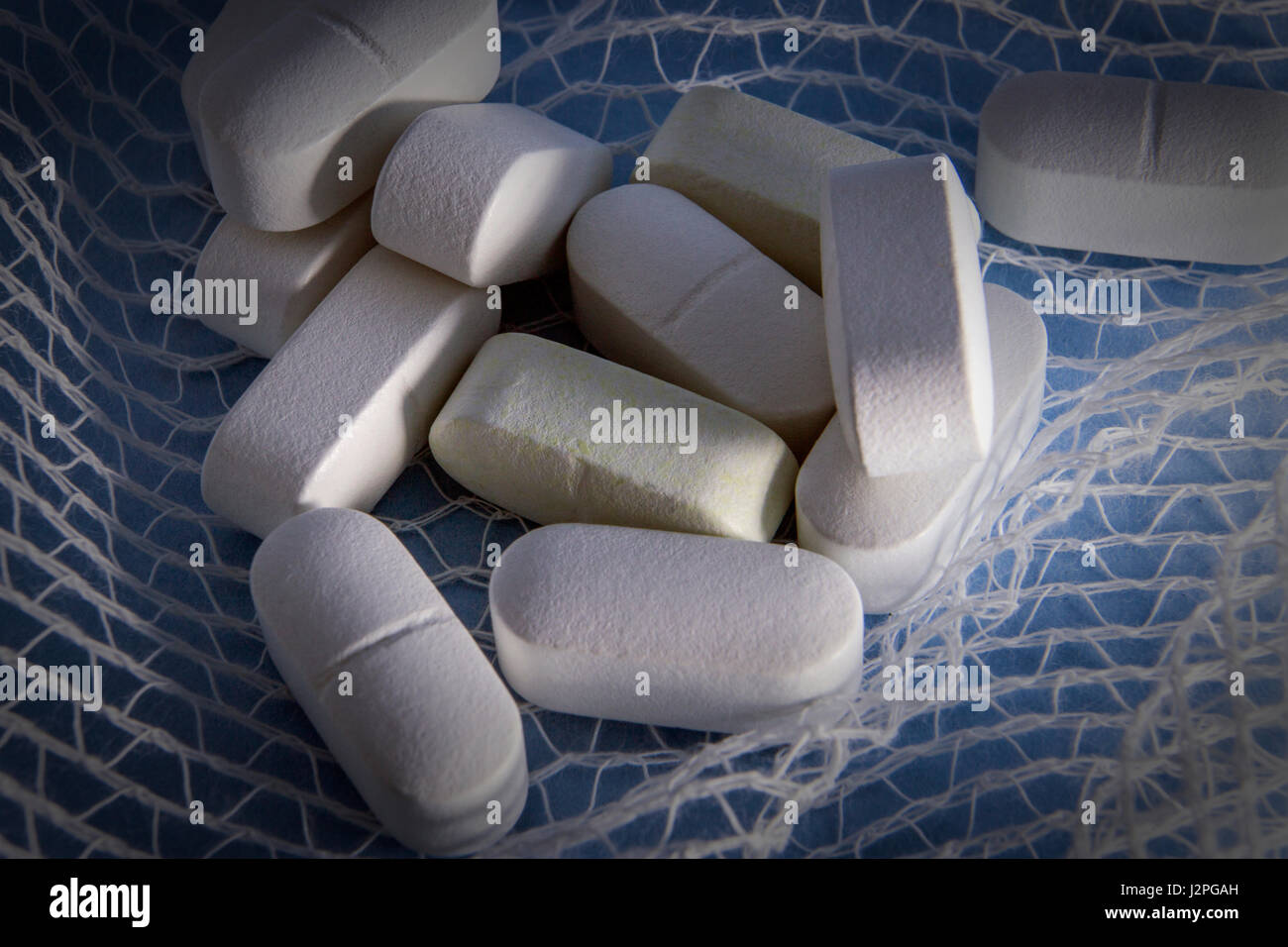 Some white pills wrapped in gauze on a blue background Stock Photo - Alamy