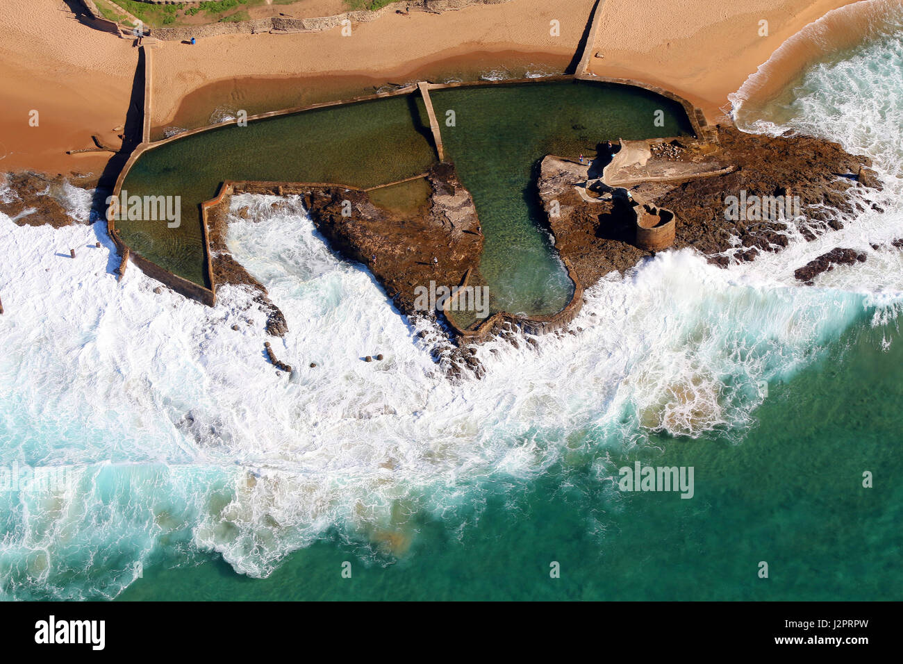 An aerial perspective of waves breaking along a rocky shoreline next to ...