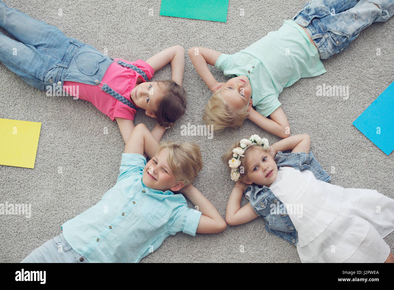 Four happy children laying on floor and smiling among colorful paper ...