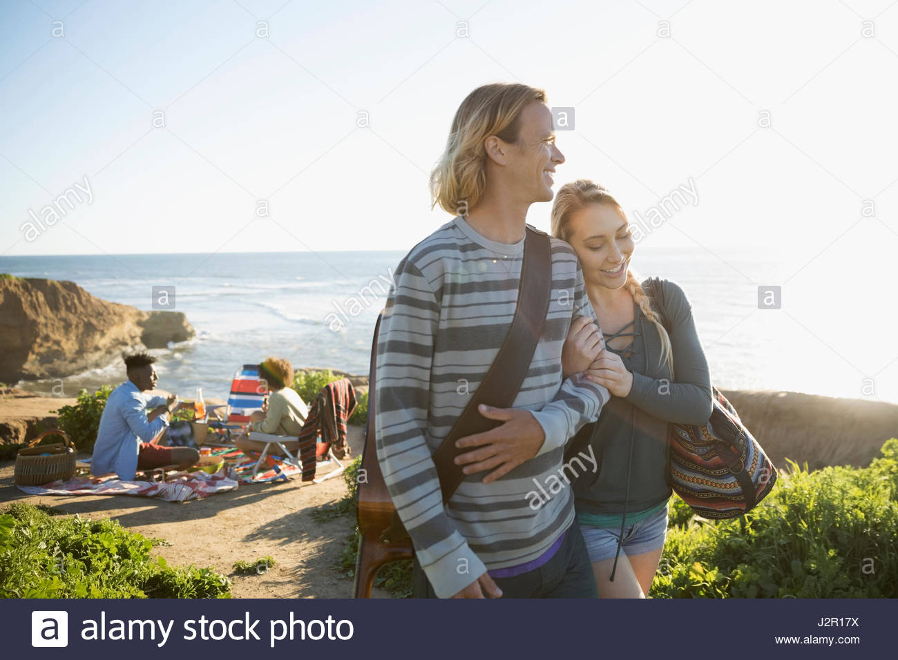 Affectionate young couple walking arm in arm with guitar on sunny beach ...