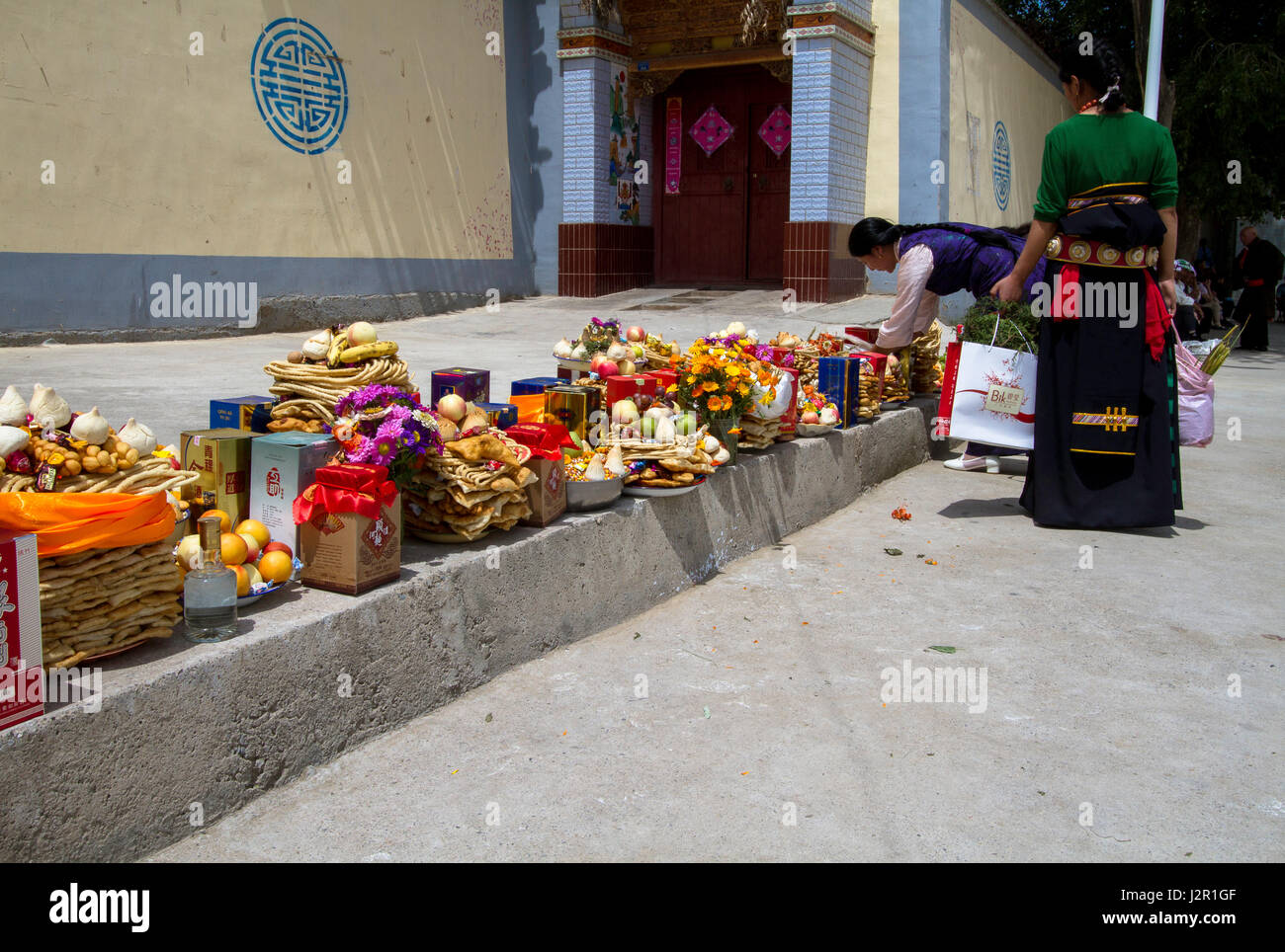 Two ethnic Tibetan women place ritual food offering at a ceremony in a ...