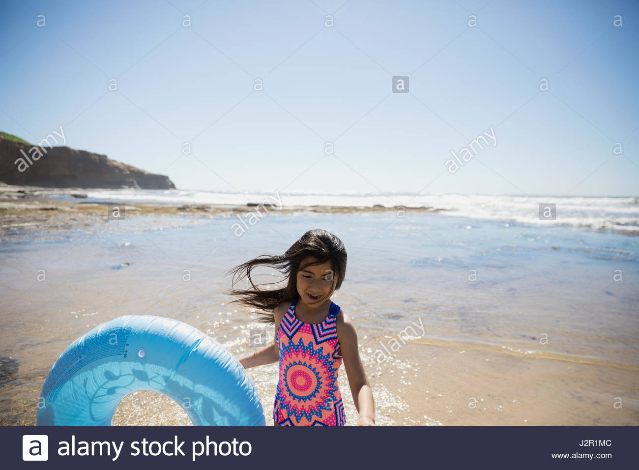 Latina girl in bathing suit holding inflatable ring on sunny beach ...