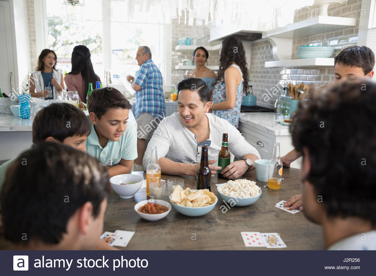Father and sons playing cards, eating and drinking at beach house ...
