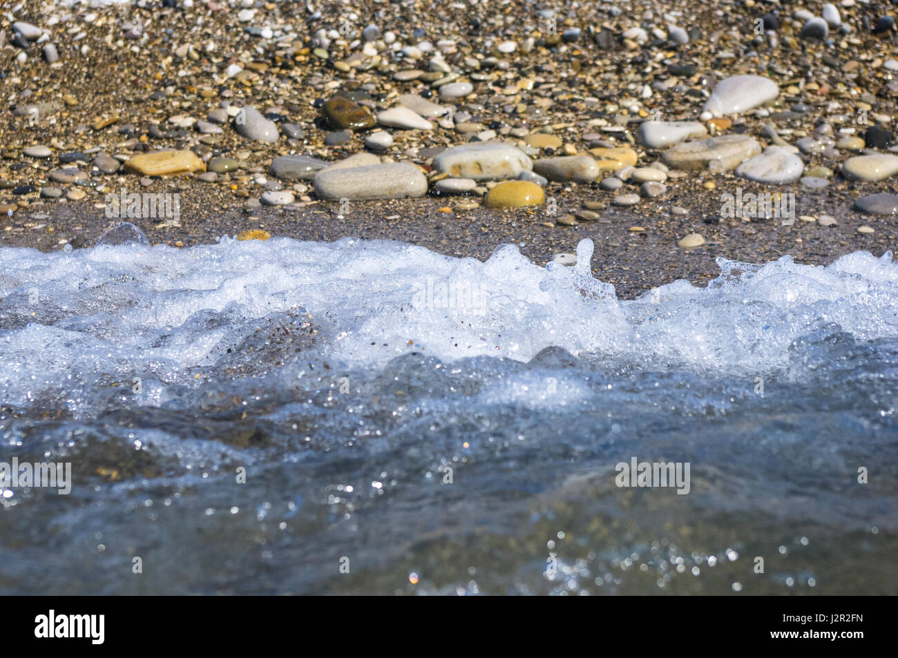 sea pebble beach with multicoloured stones, transparent waves with foam ...