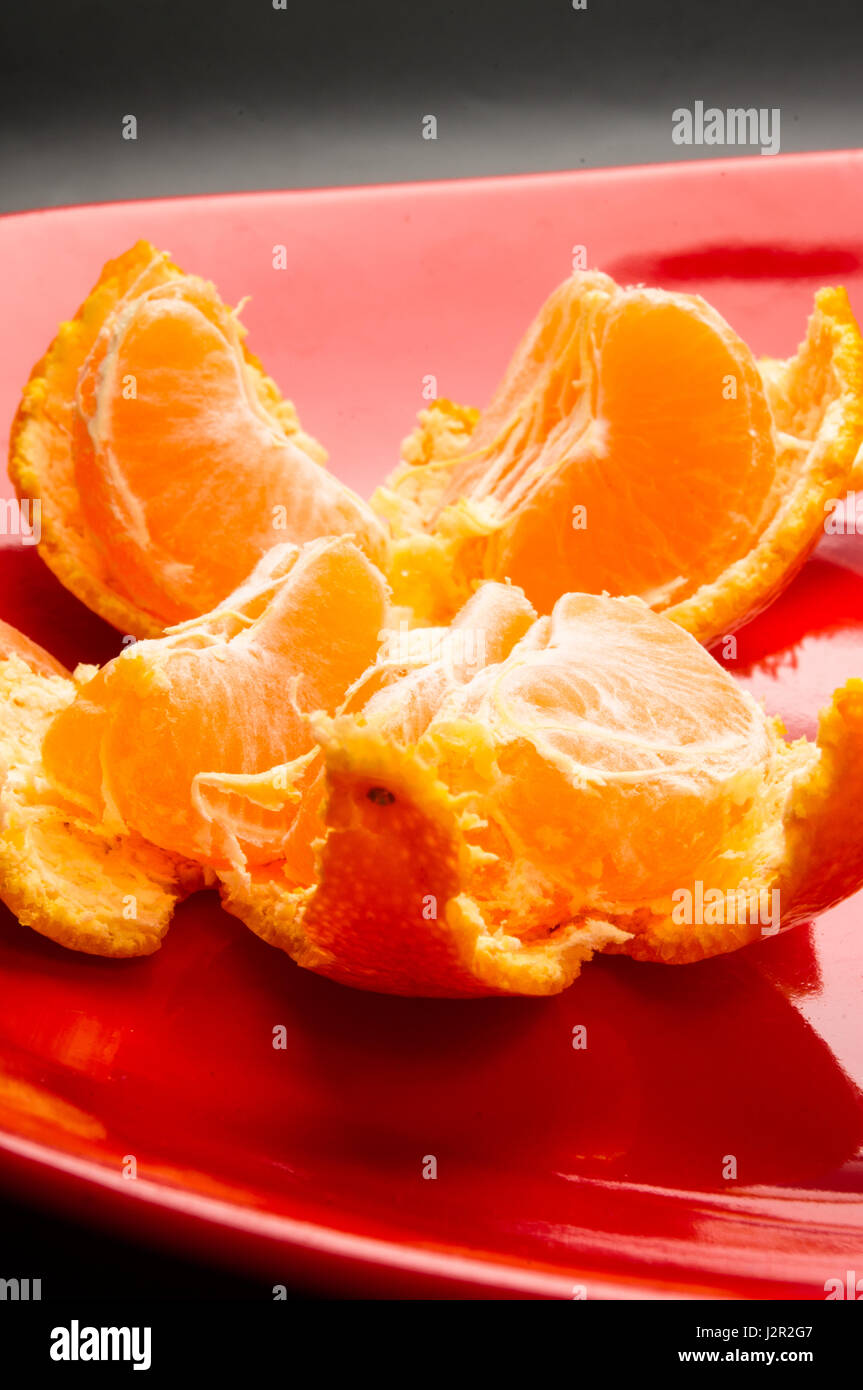 tangerines, peeled tangerine and tangerine slices in a red plate on ...