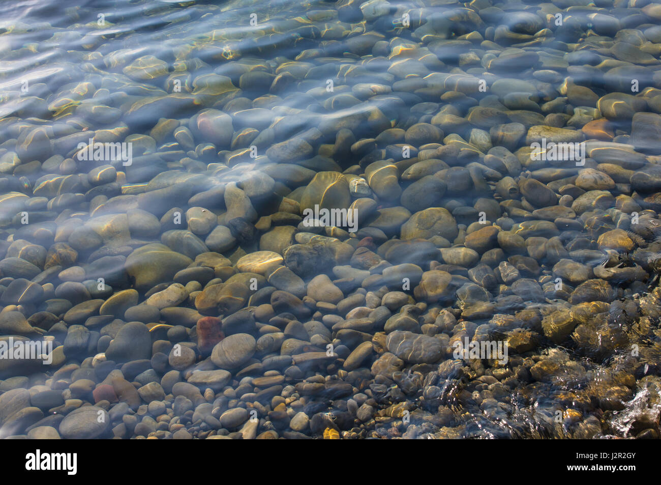 sea pebble beach with multicoloured stones, transparent waves with foam ...