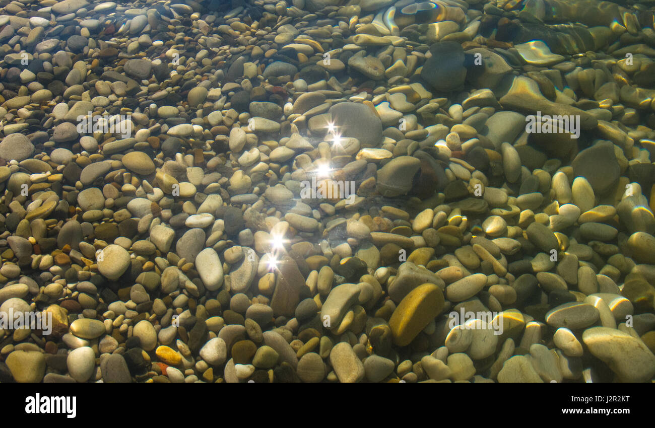 sea pebble beach with multicoloured stones, transparent waves with foam ...