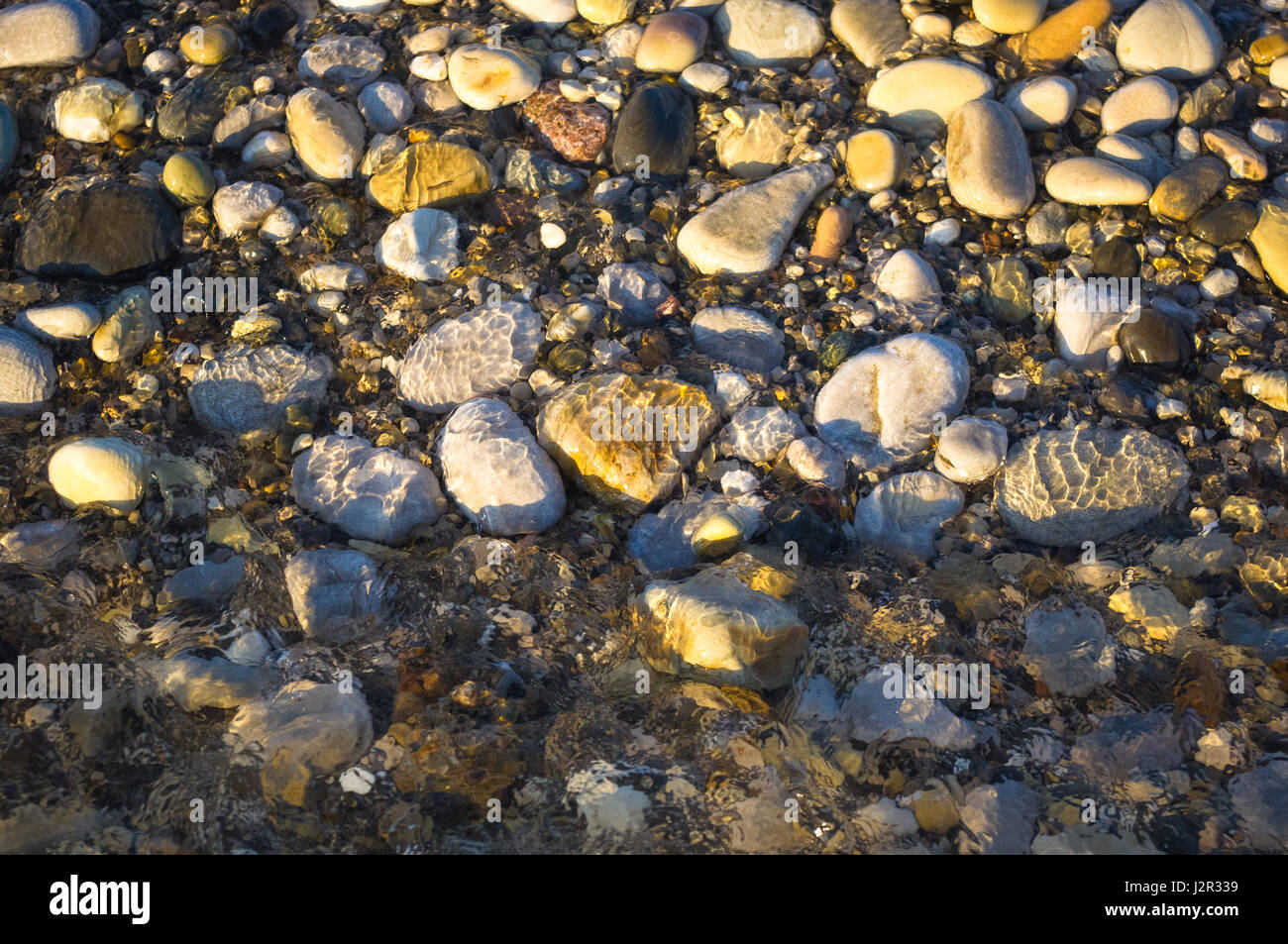 sea pebble beach with multicoloured stones, transparent waves with foam ...