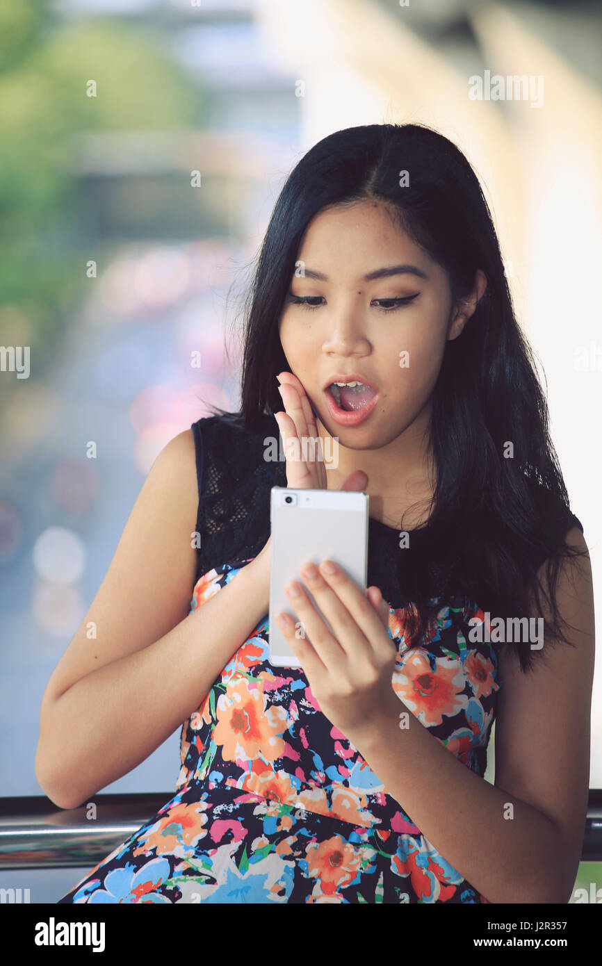 Asian woman looking surprised at her mobile phone Stock Photo - Alamy