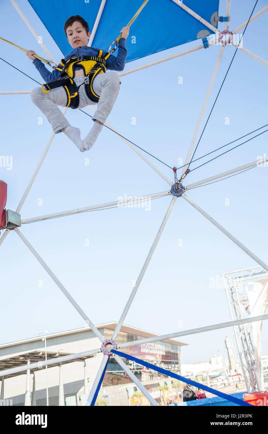 A young boy bouncing on a trampoline with bungie ropes attached to ...