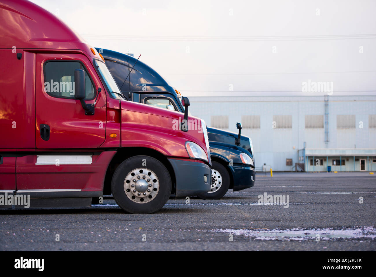 Two semi trucks of different colors stand in a row at the parking area ...