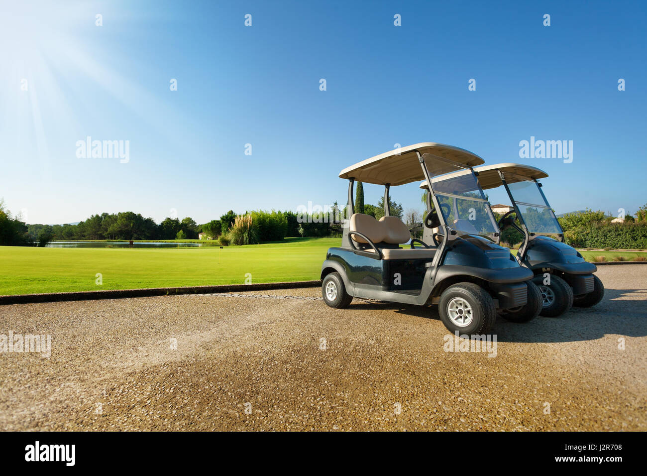 Two golf-carts standing at the parking lots against green golf course ...