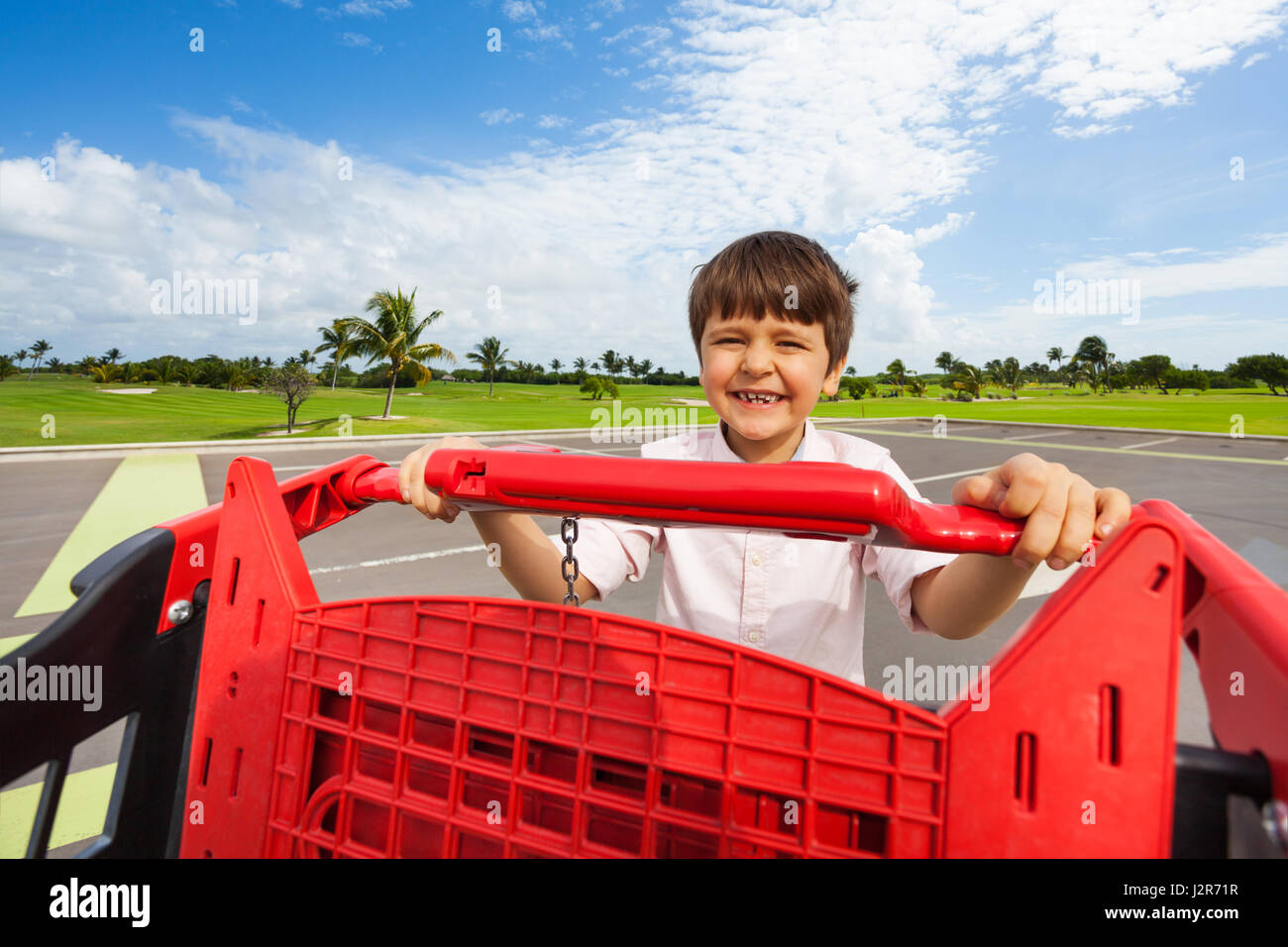 Portrait of happy kid boy pushing big red plastic shopping cart at ...