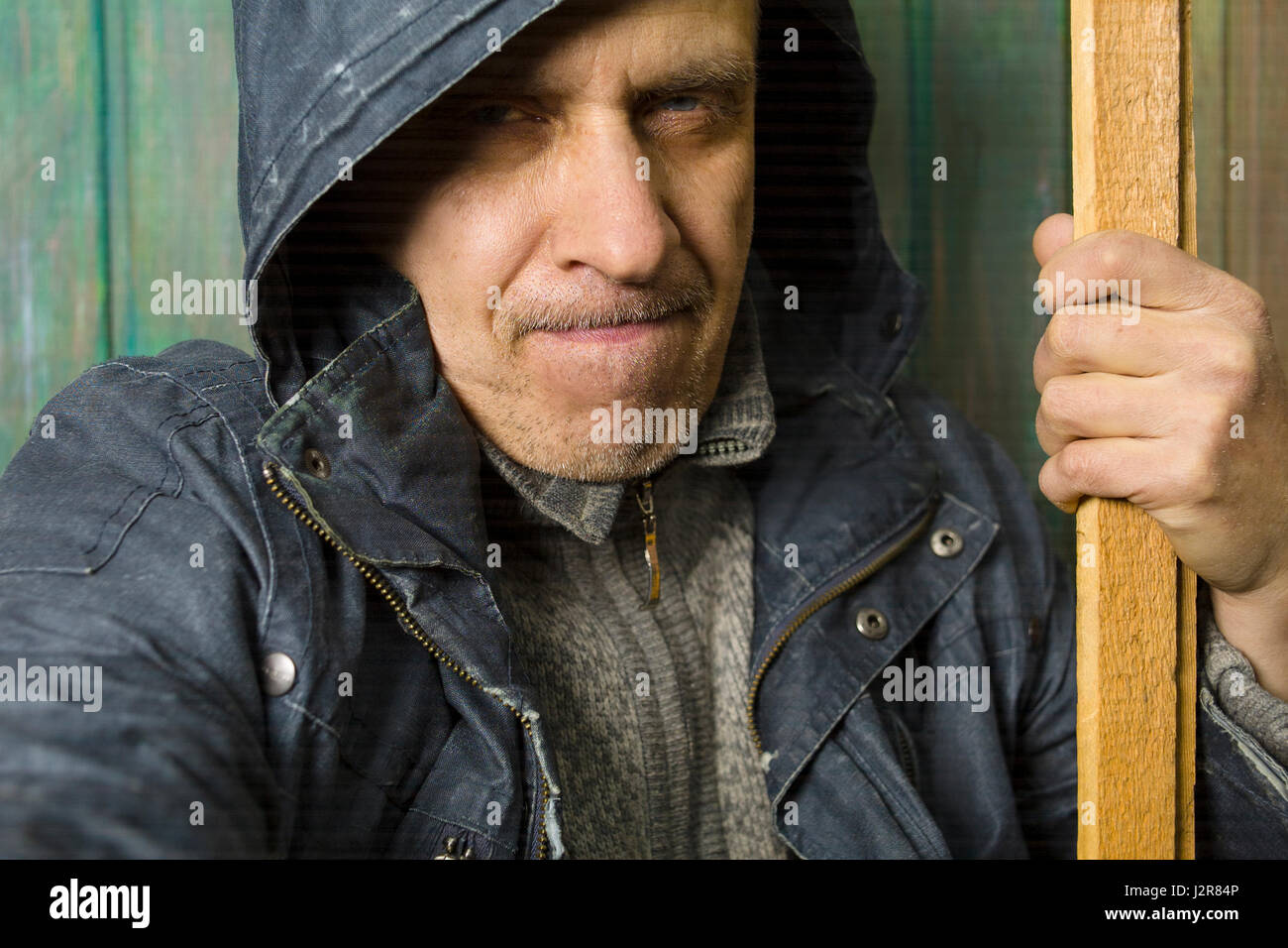 Man with a sullen look holding a wooden stick in a hand, studio ...