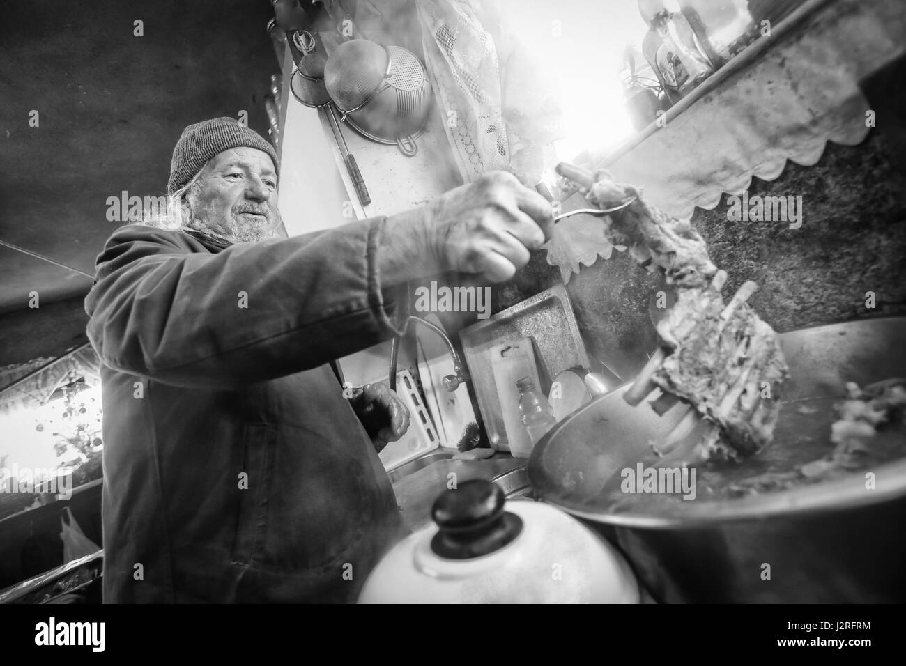 An old man boiling pork meat on the stove and holding a piece of ribs ...