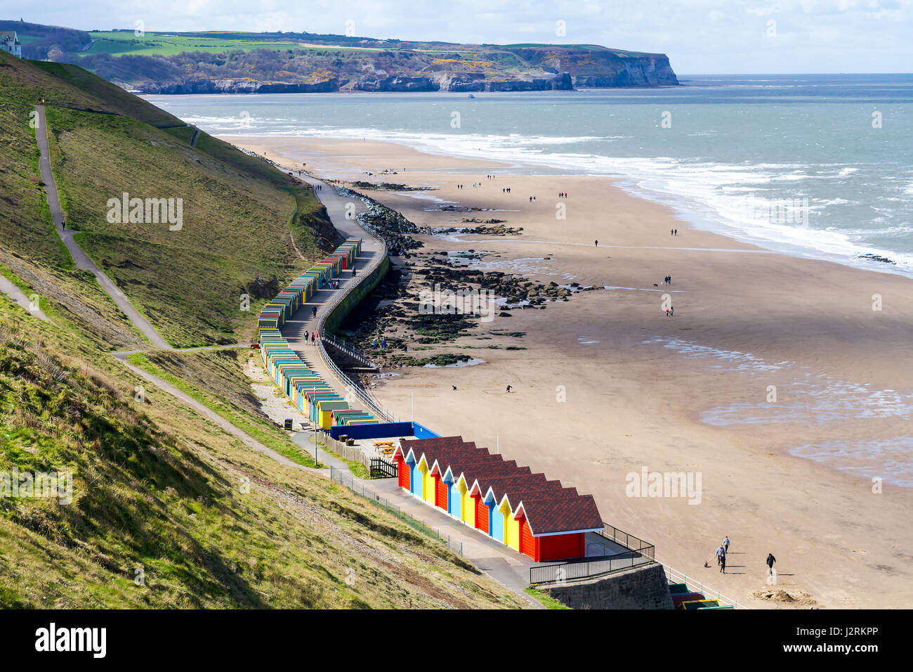Row of brightly coloured wooden beach huts curving along the West Cliff ...