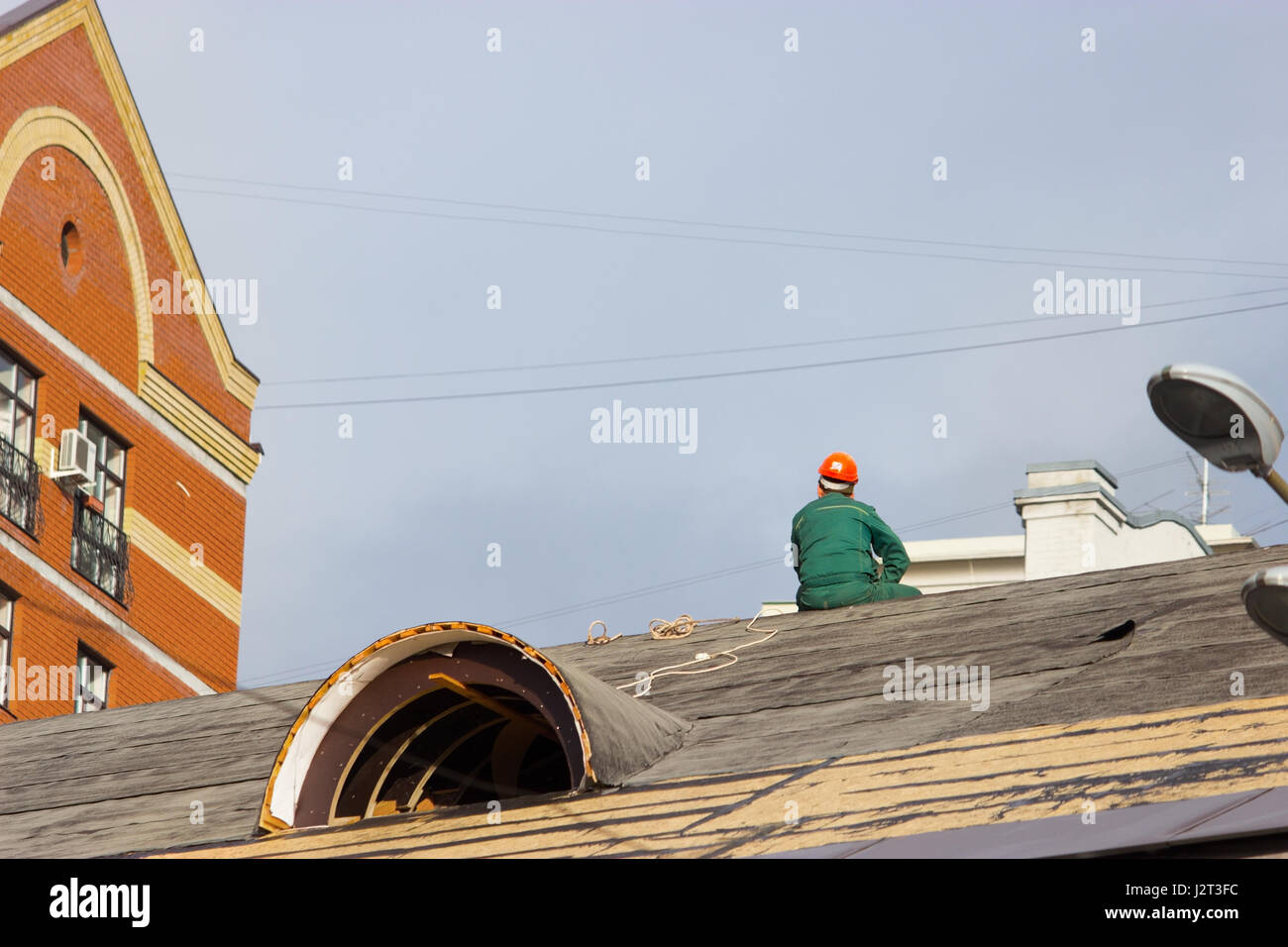 worker in a helmet sit on the building roof Stock Photo - Alamy