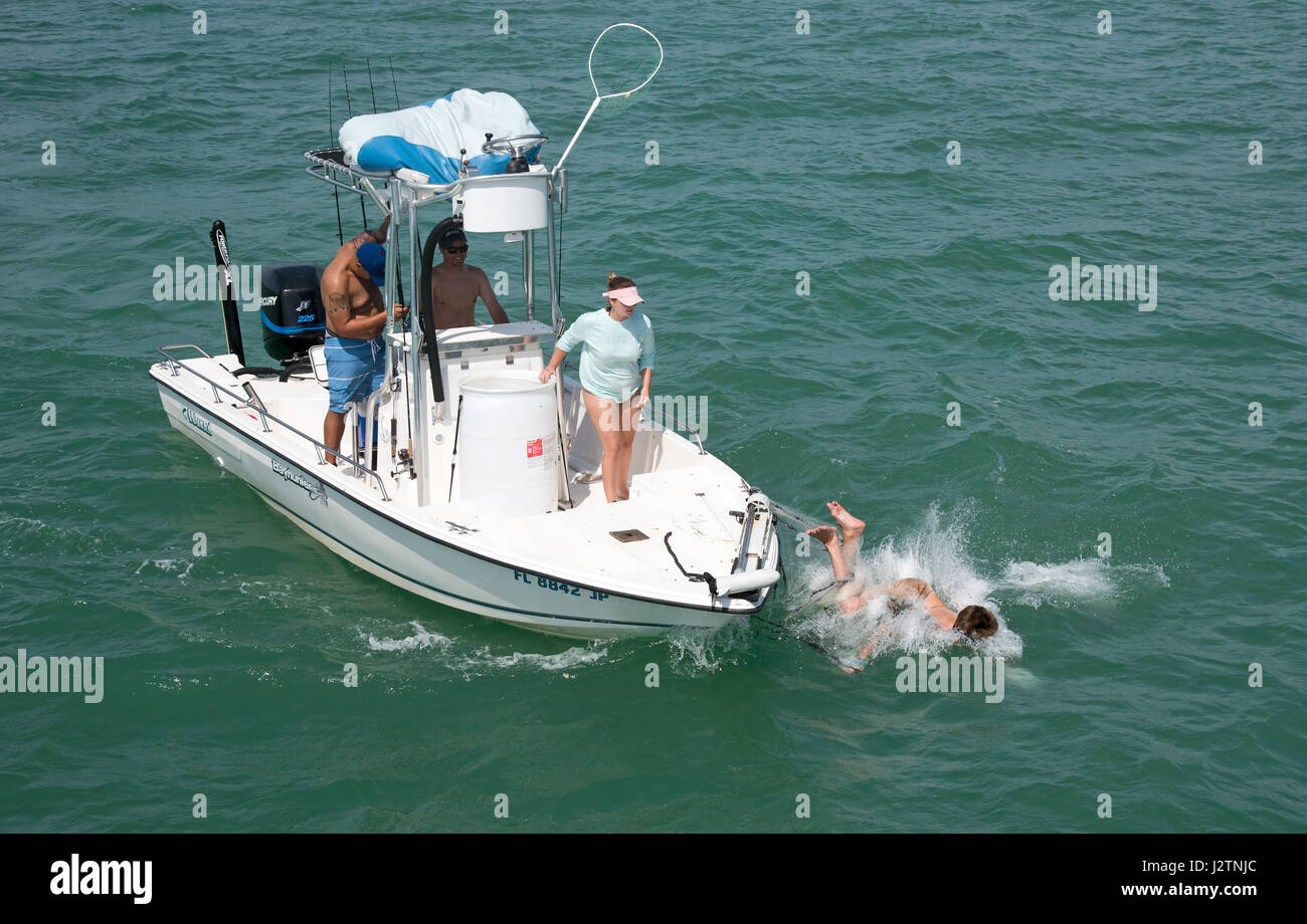 A young man fishing for bait using a cast net falls from the boat with ...