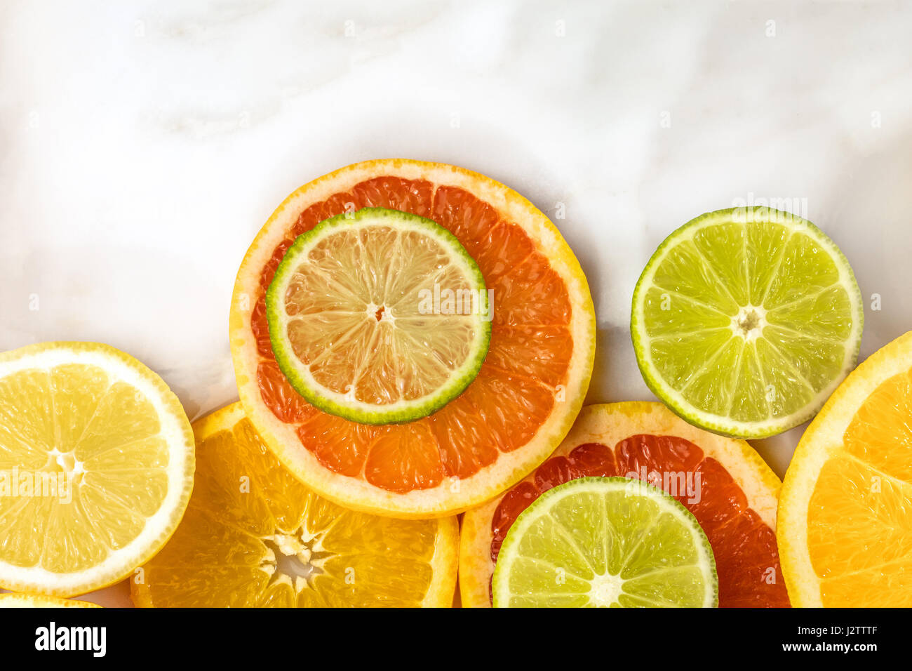 Vibrant juicy citrus fruits on a white marble texture with copy space ...