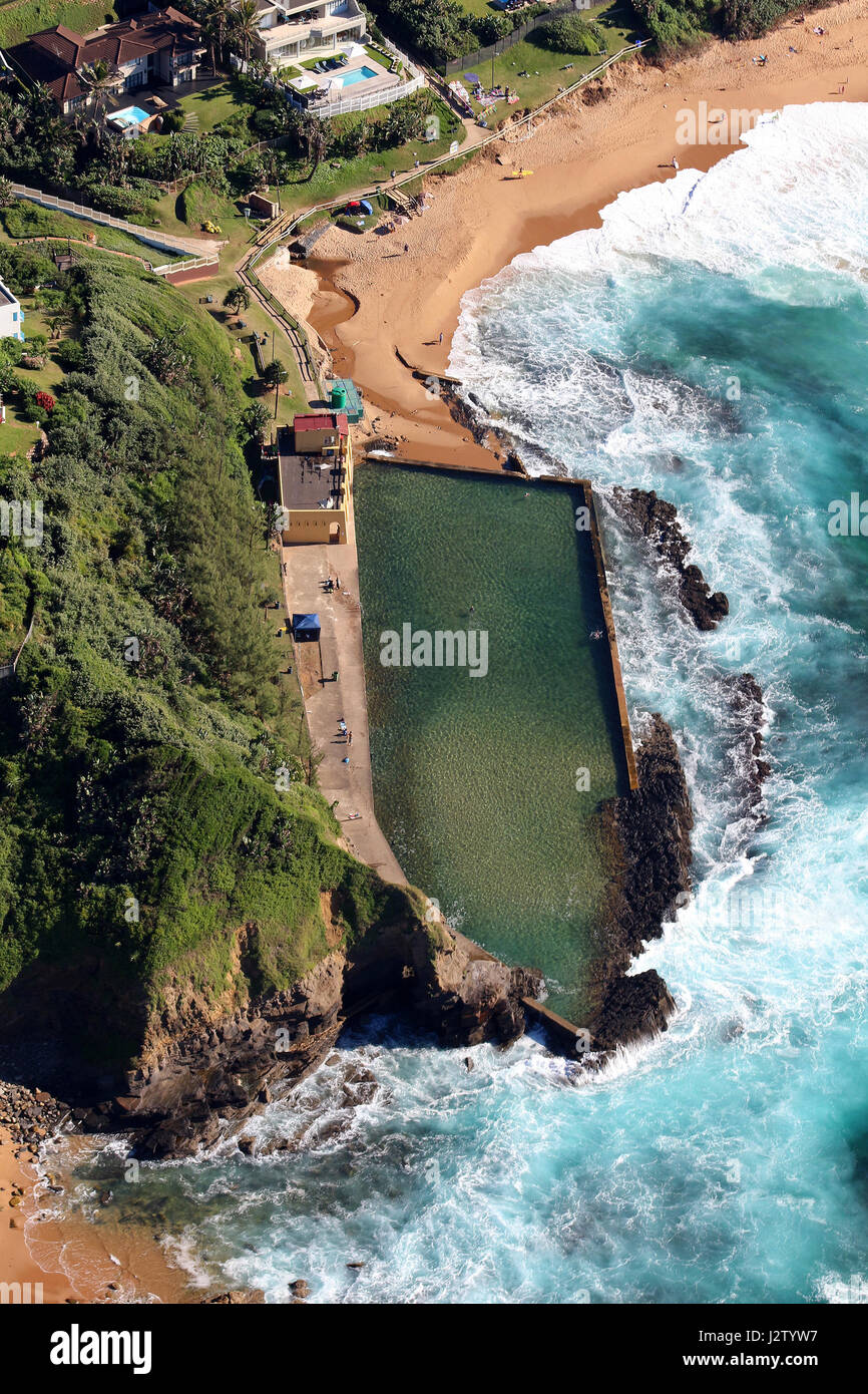 An aerial perspective of waves breaking along a rocky shoreline next to ...