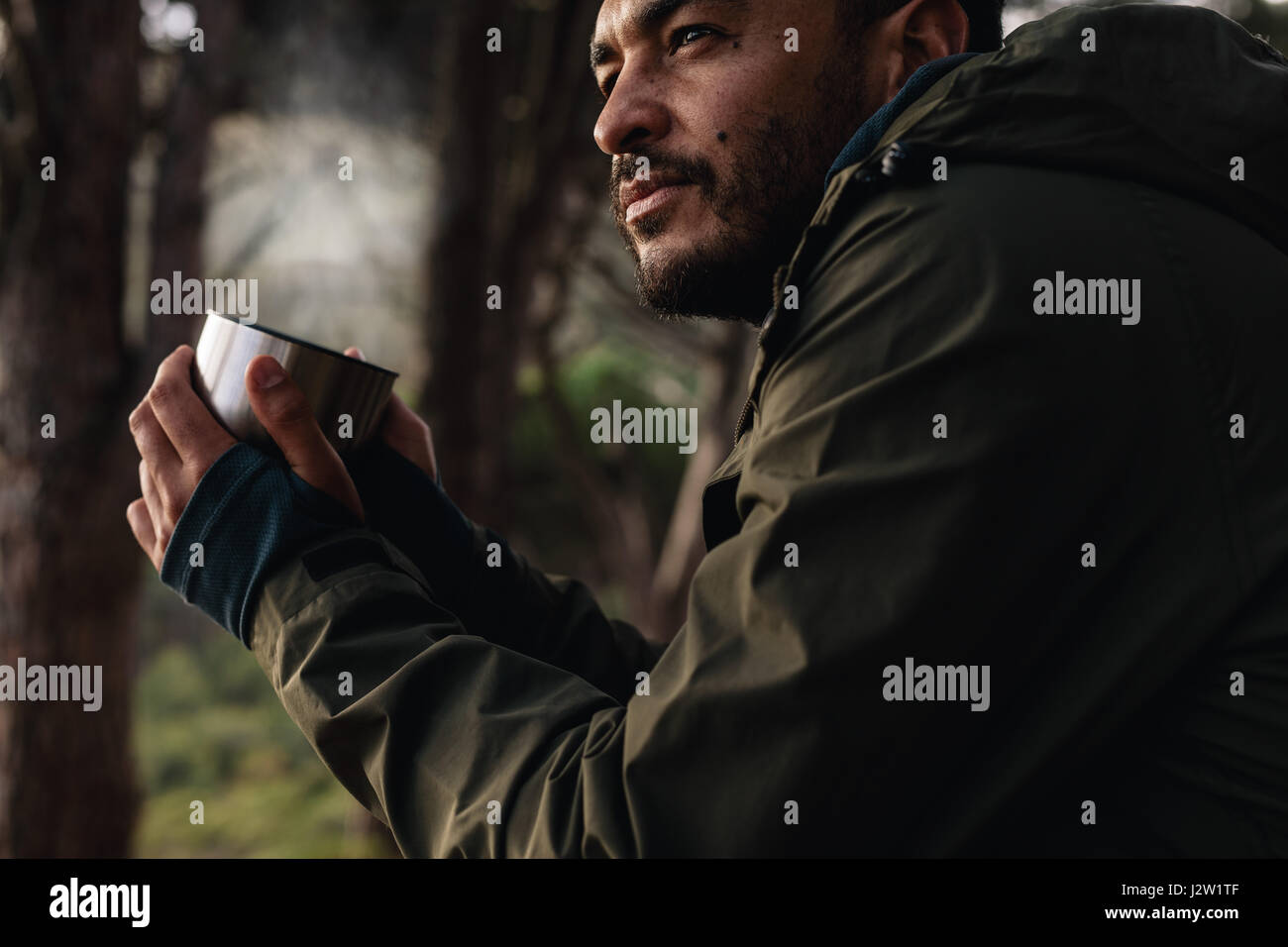 Close up shot of relaxed young man having coffee outdoors. Male hiker ...