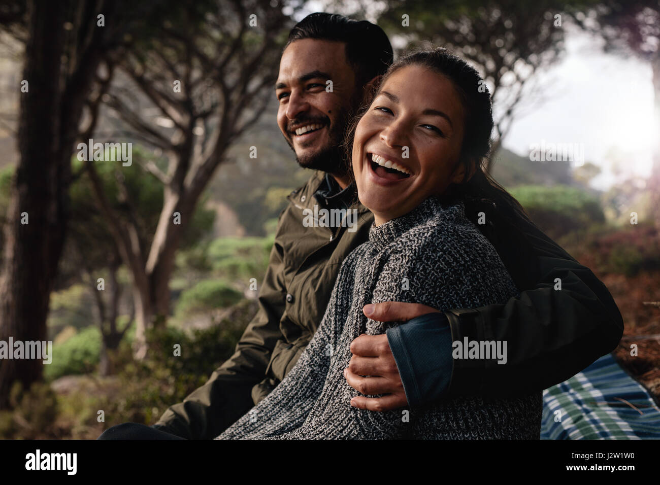 Young asian woman sitting outdoors with her boyfriend and smiling. Young hiker couple resting ...