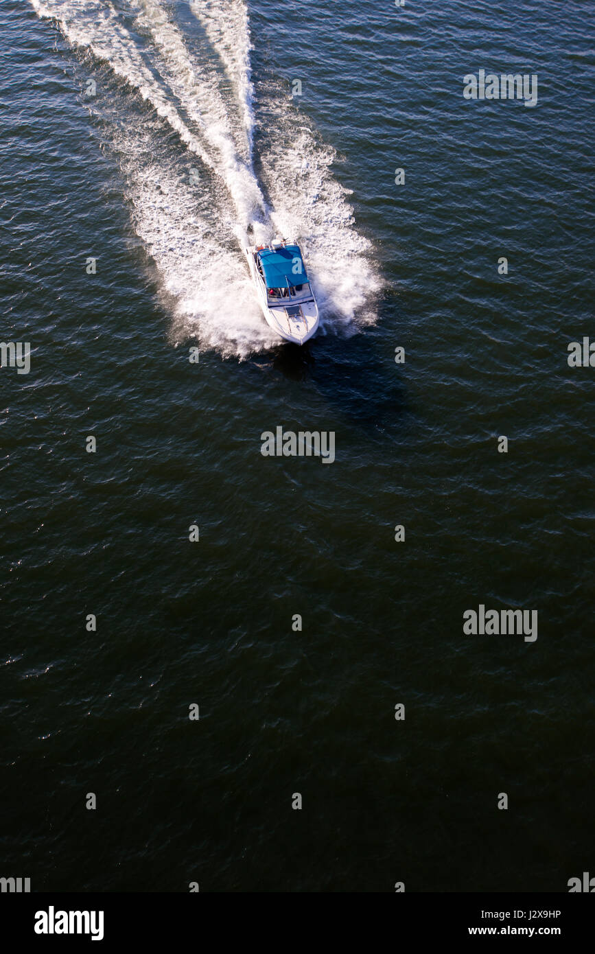 Fast motor boat with white blue canopy rushes through the dark surface ...