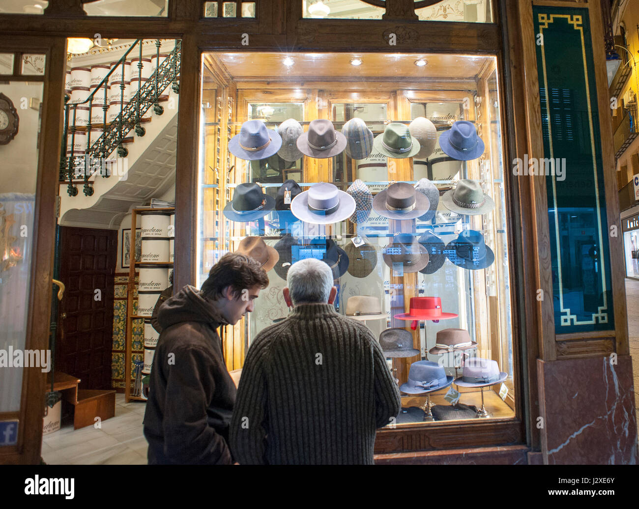 young man and elderly man in front of window of a traditional hat shop ...