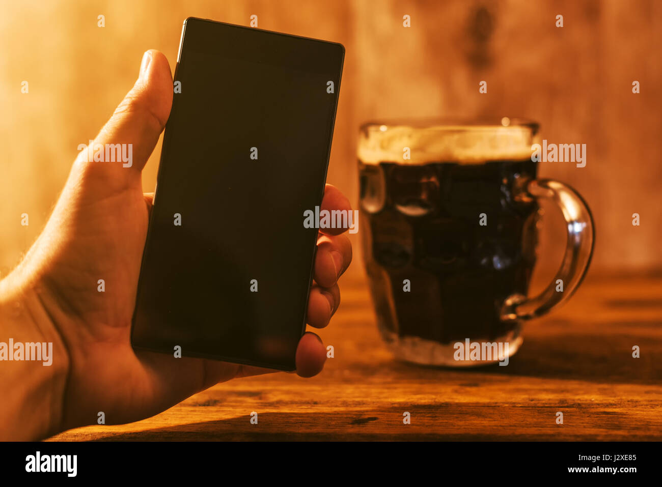 Man with mobile phone and dark beer mug sitting in the bar, drinking ...
