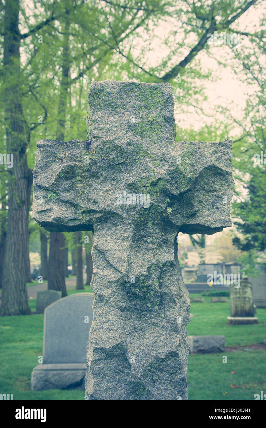 A stone cross tombstone with moss covering it in an old cemetery Stock ...