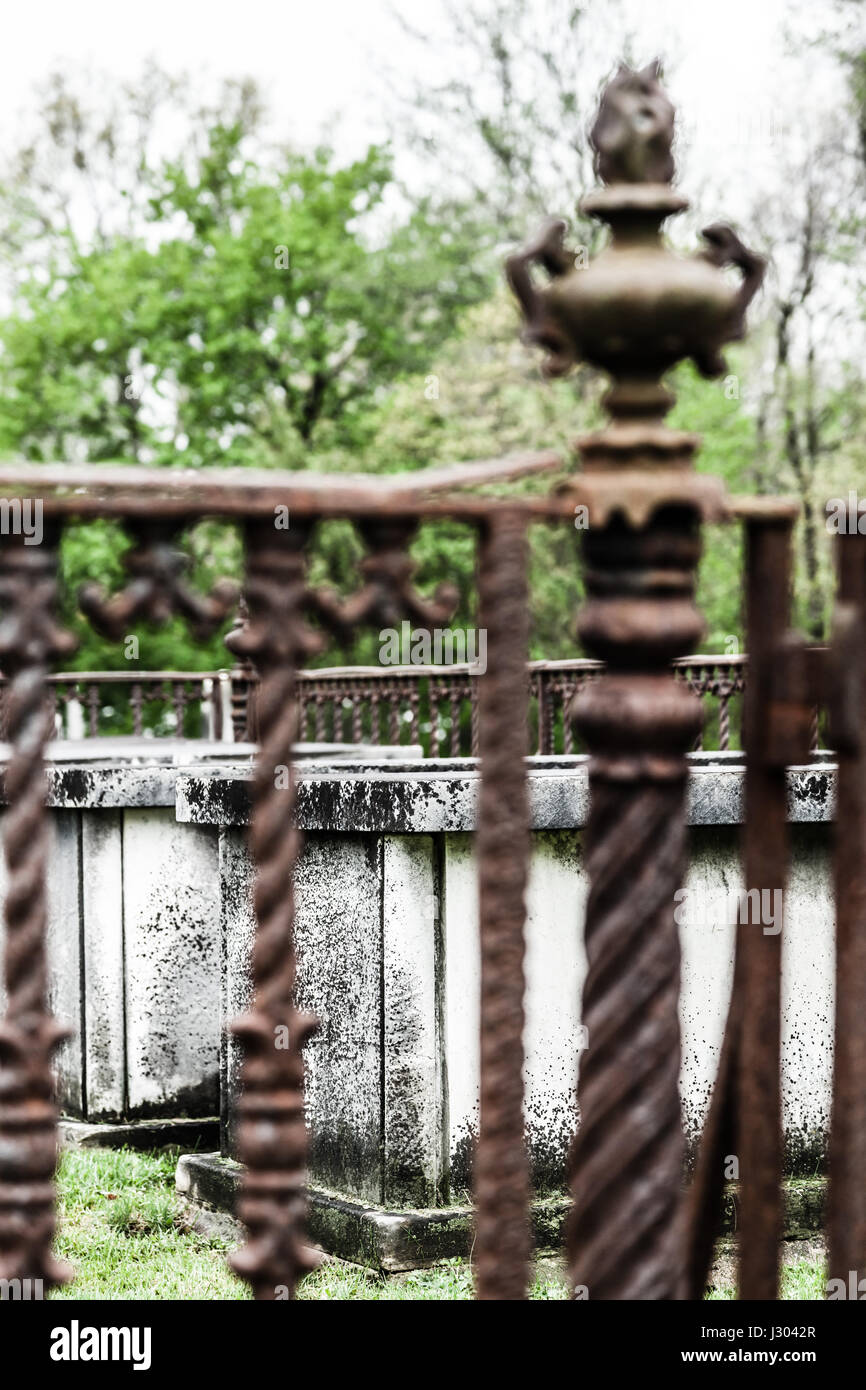 An old weathered crypt sits inside a metal fenced in area in a cemetery ...