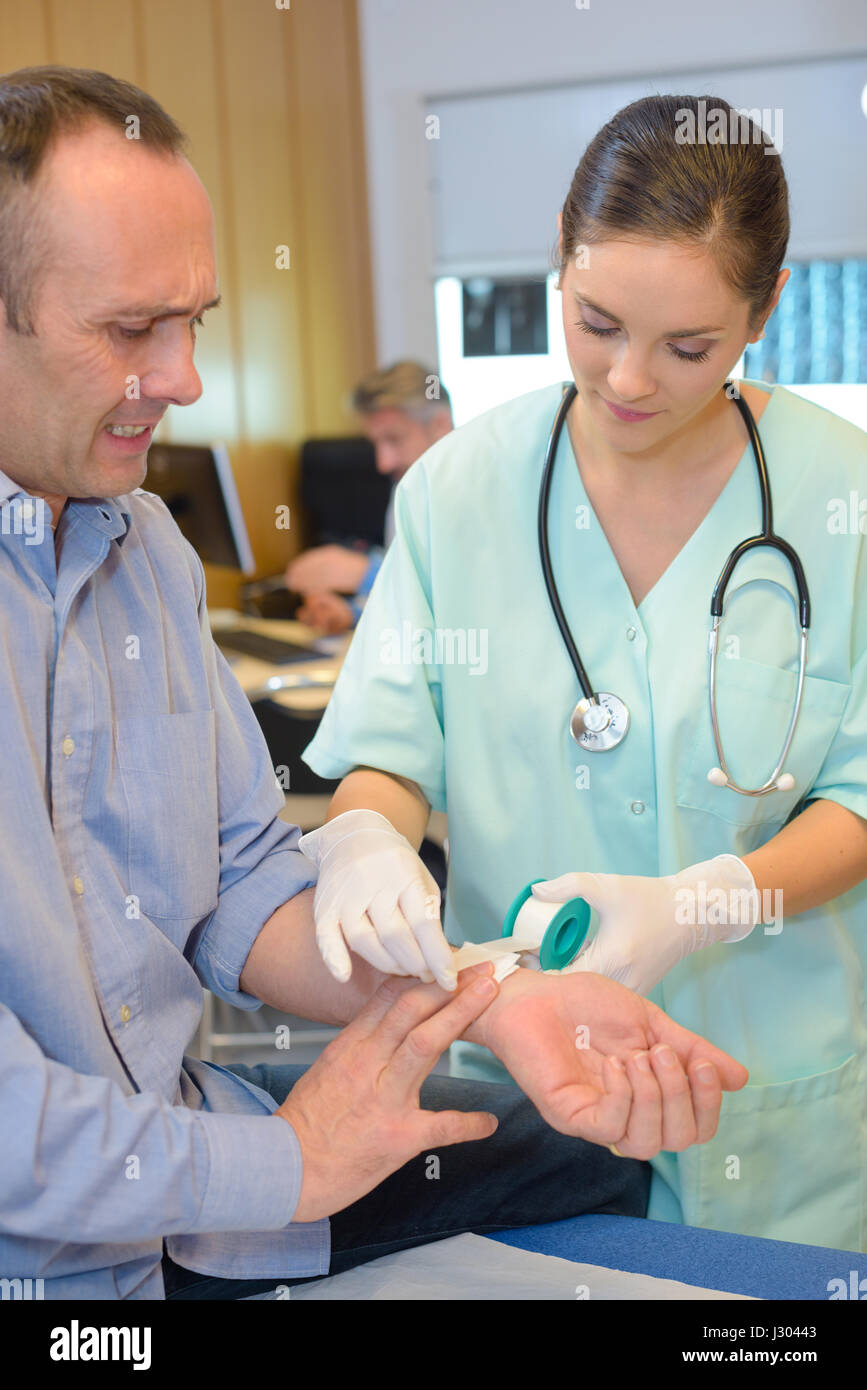 Man wincing as nurse applies tape to wrist Stock Photo - Alamy