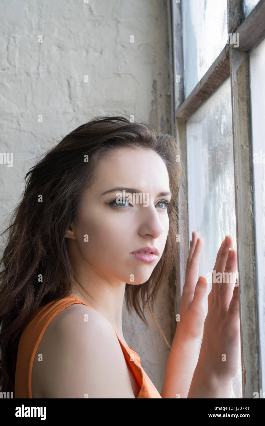 Serious young woman hands touching the glass looking out of the window ...