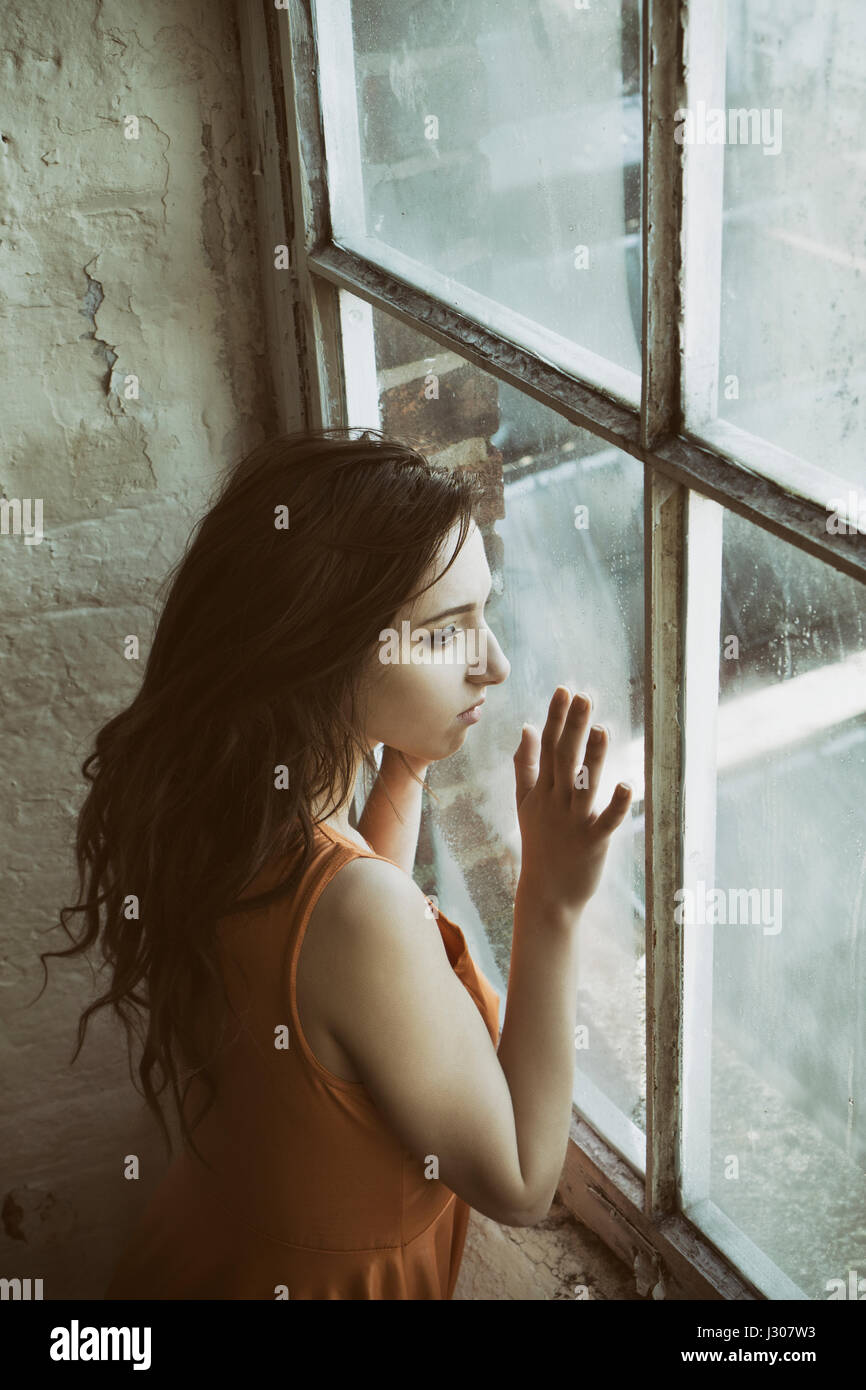 Sad young woman standing by the window hands touching the glass Stock ...