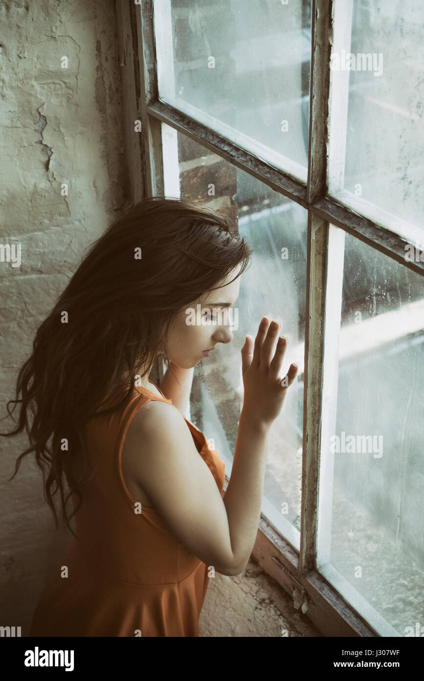 Sad young woman standing by the window hands touching the glass Stock ...