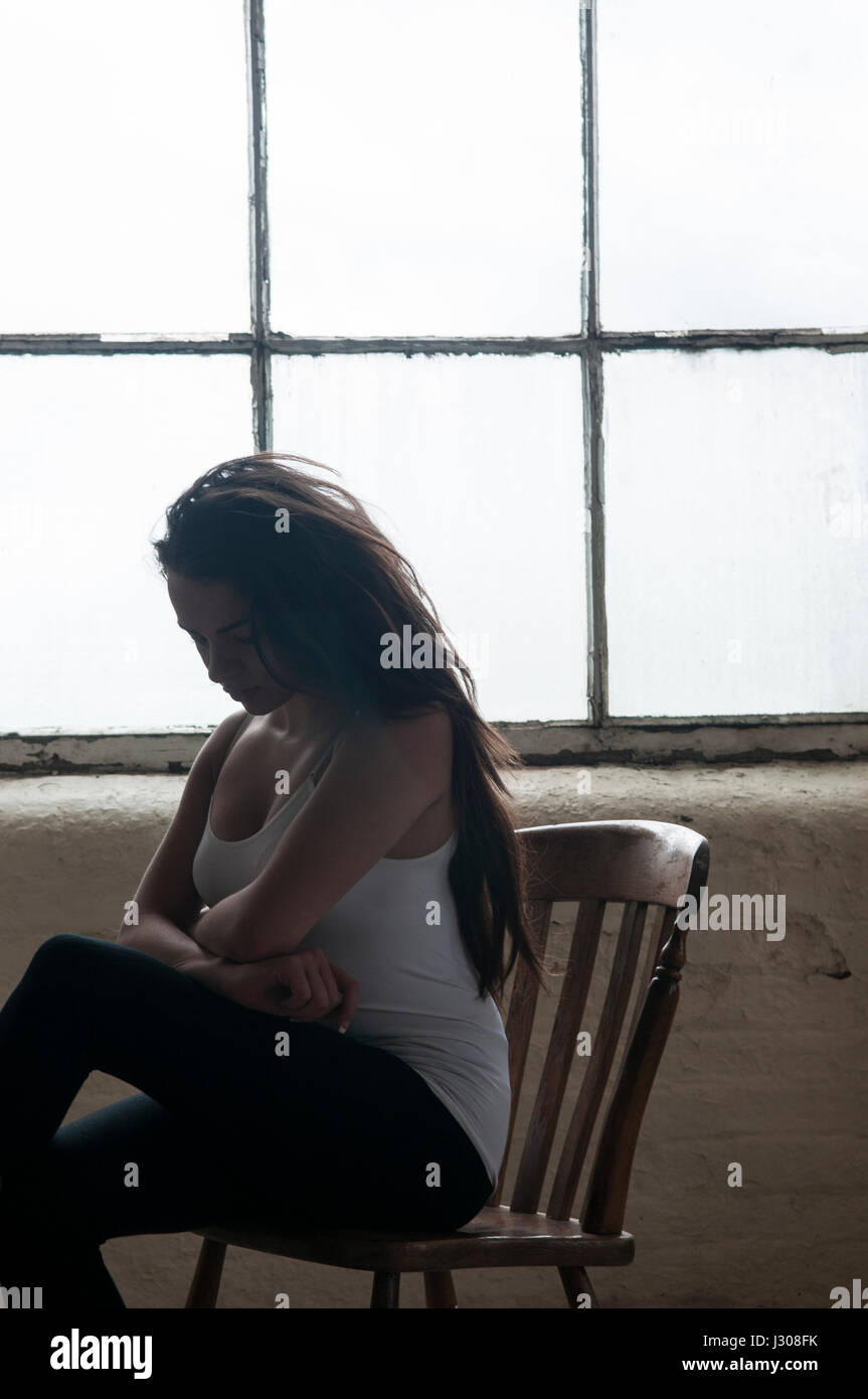 Sad young woman sat on chair near the window Stock Photo - Alamy