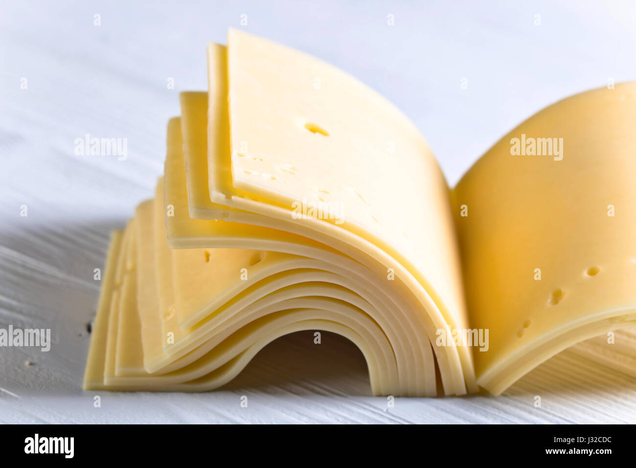Slices of cheese folded like a book on a white wooden table Stock Photo ...