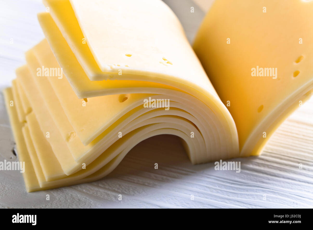 Slices of cheese folded like a book on a white wooden table Stock Photo ...